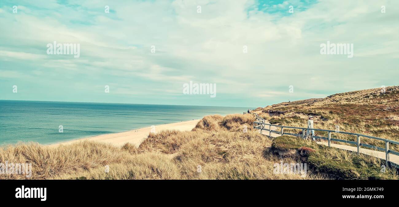 An elevated grassy coast with a wooden boardwalk under a cloudy sky ...