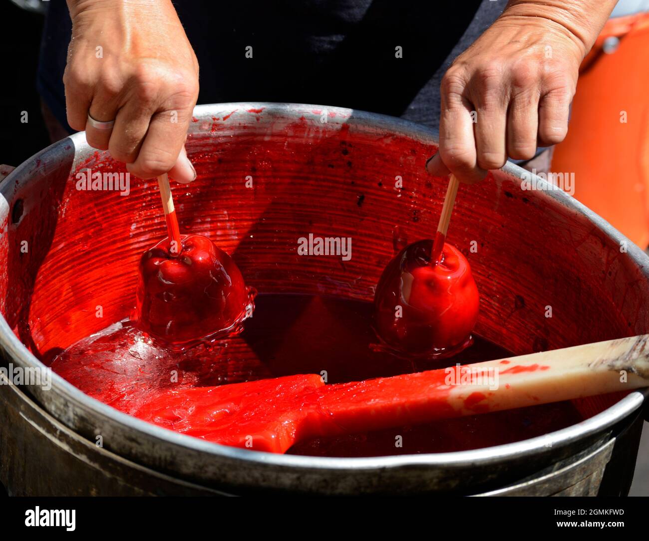 A worker at a food vendor booth dips apples to make candy apples ...