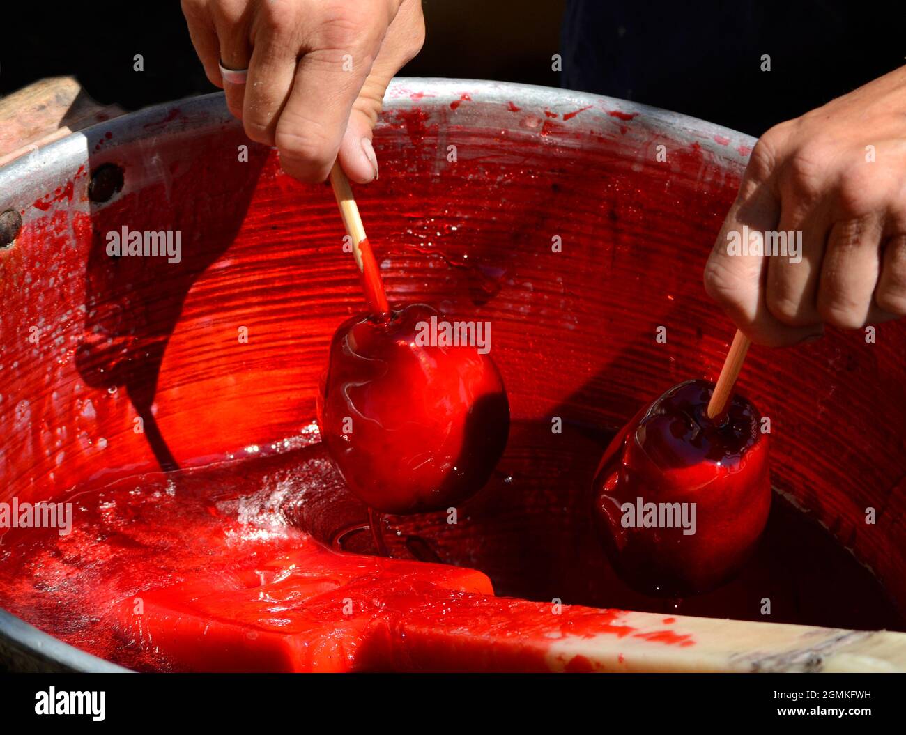 A worker at a food vendor booth dips apples to make candy apples ...