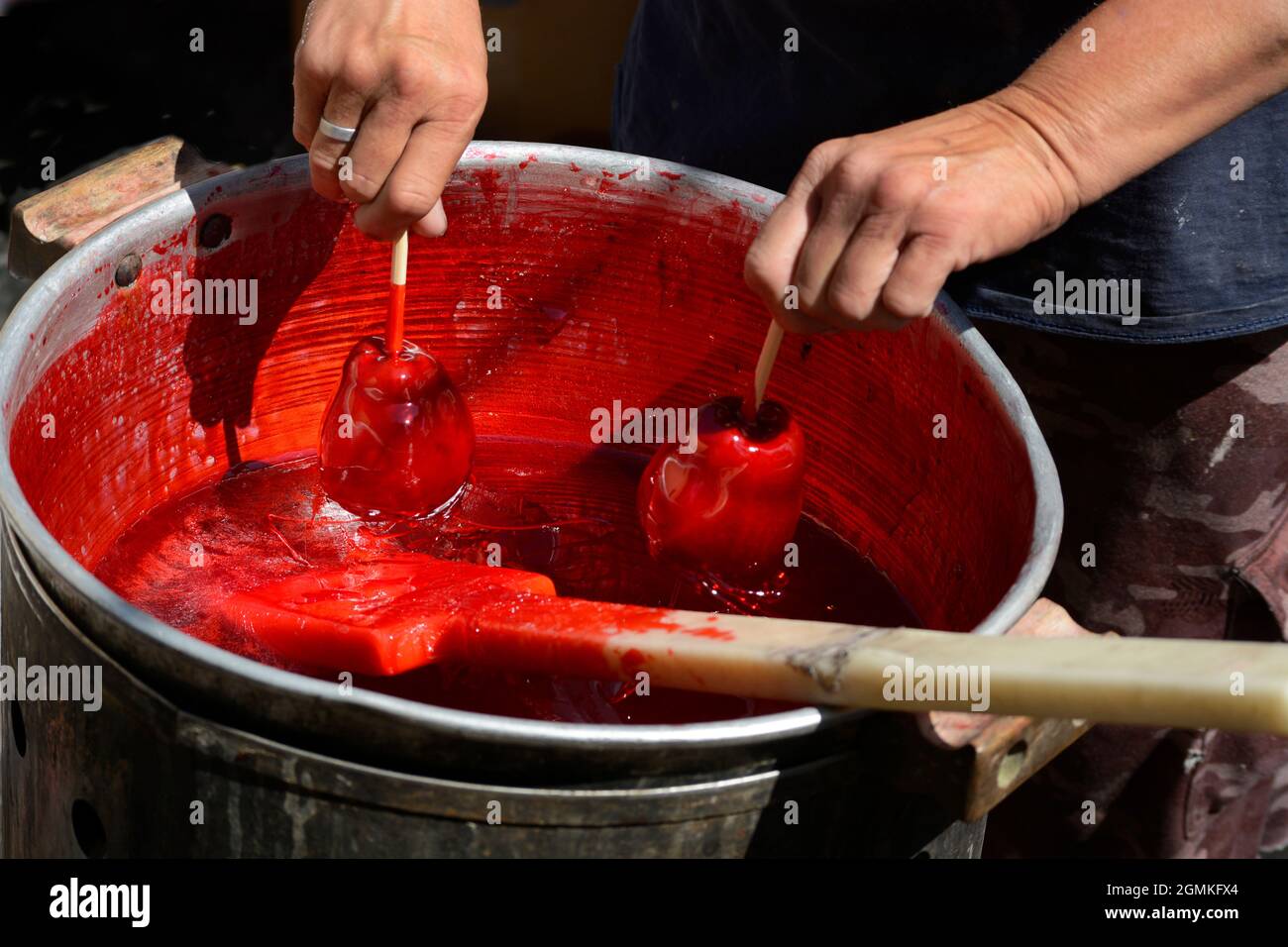 A worker at a food vendor booth dips apples to make candy apples ...