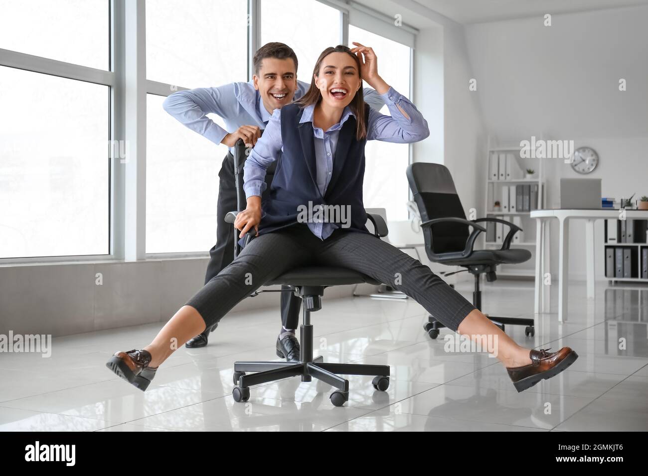 Happy colleagues riding chair in office Stock Photo - Alamy