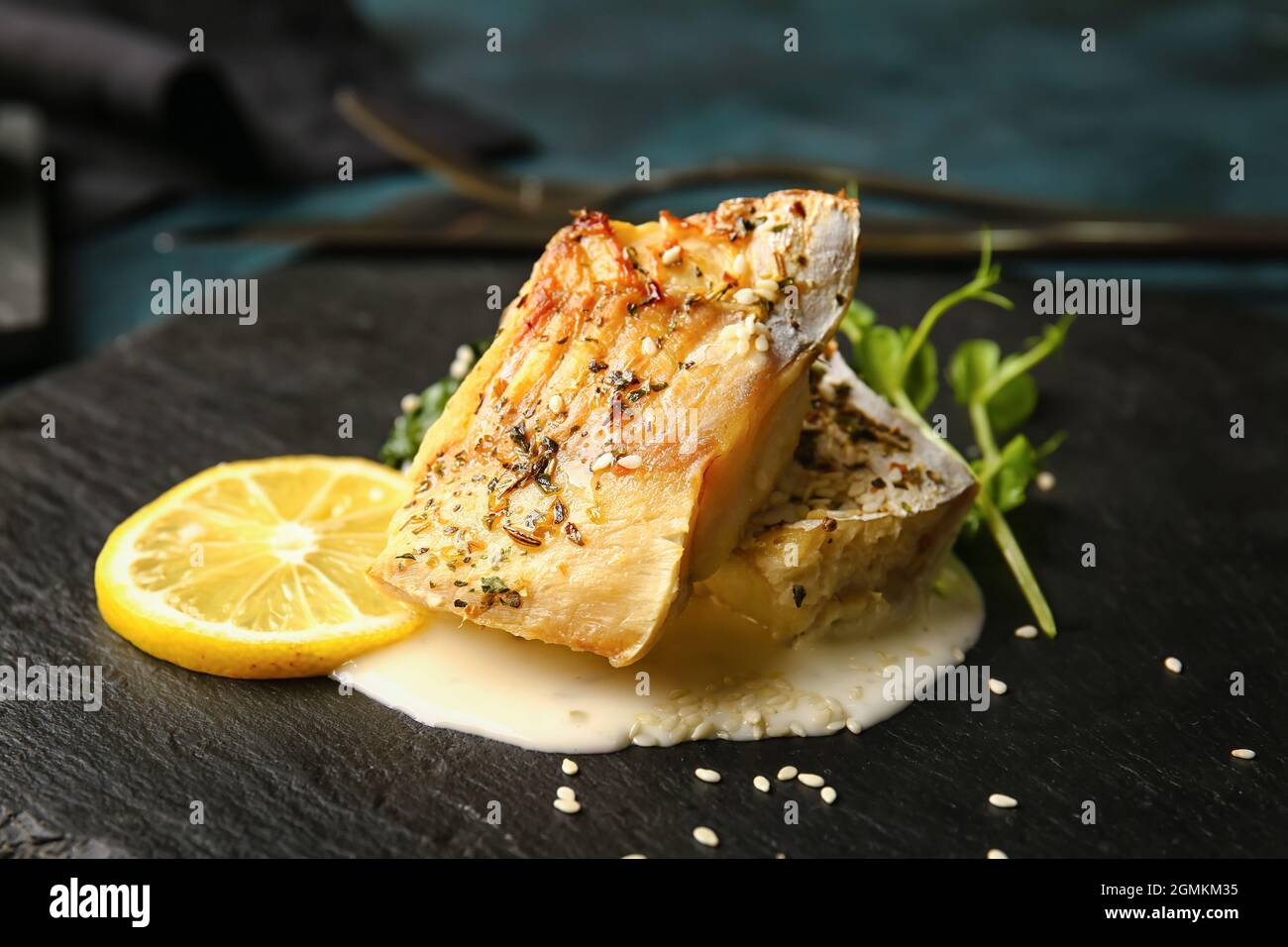 Board with tasty baked cod fillet, sauce and lemon on dark background ...