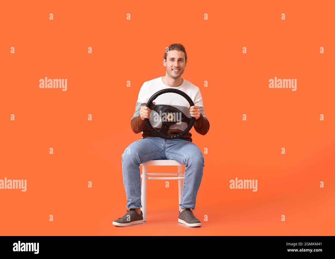 Young man with steering wheel sitting on chair against color background ...