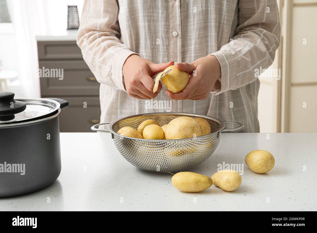 Woman peeling raw potatoes at table in kitchen, closeup Stock Photo - Alamy