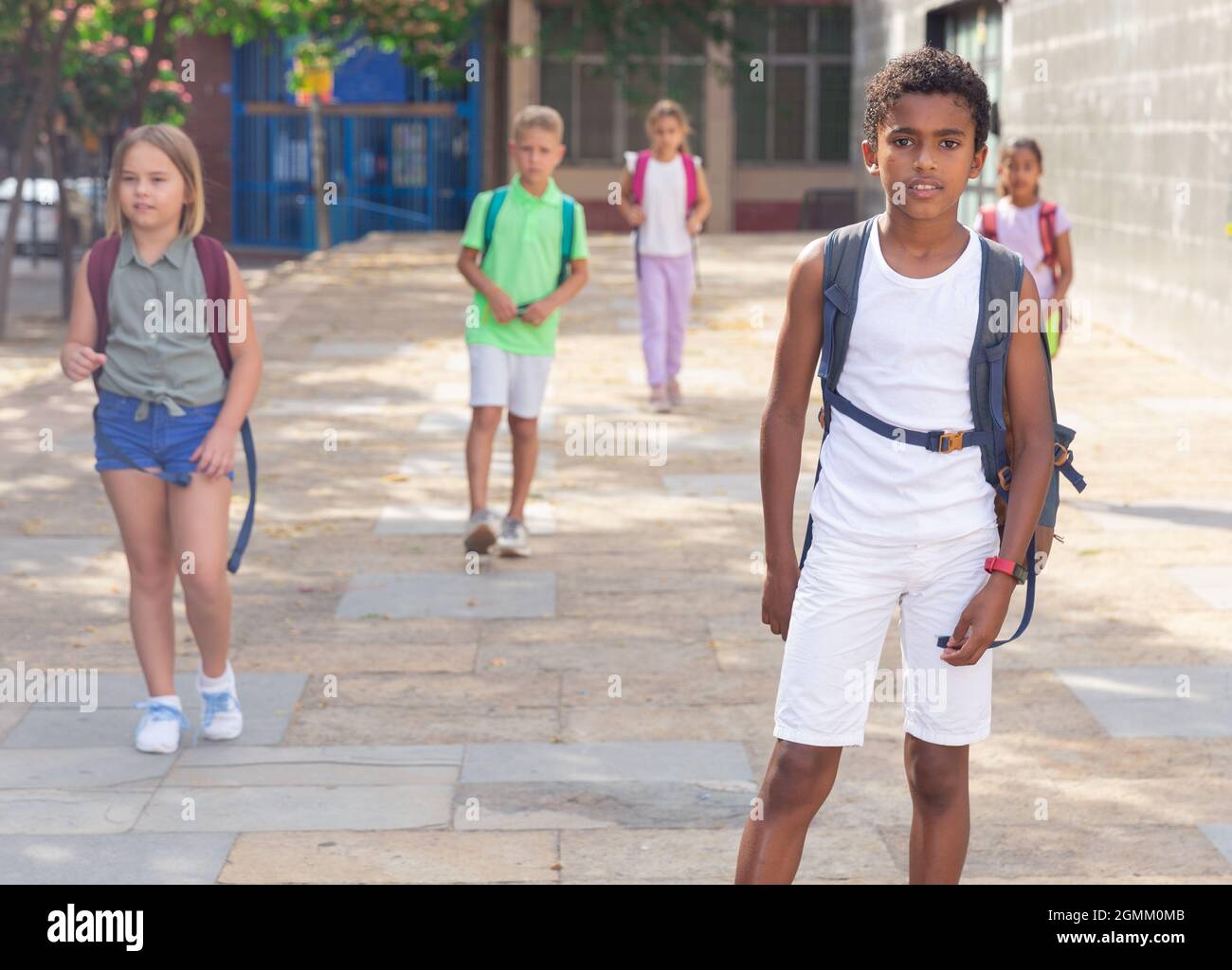 Portrait of smiling schoolboy walking on street, kids on background ...