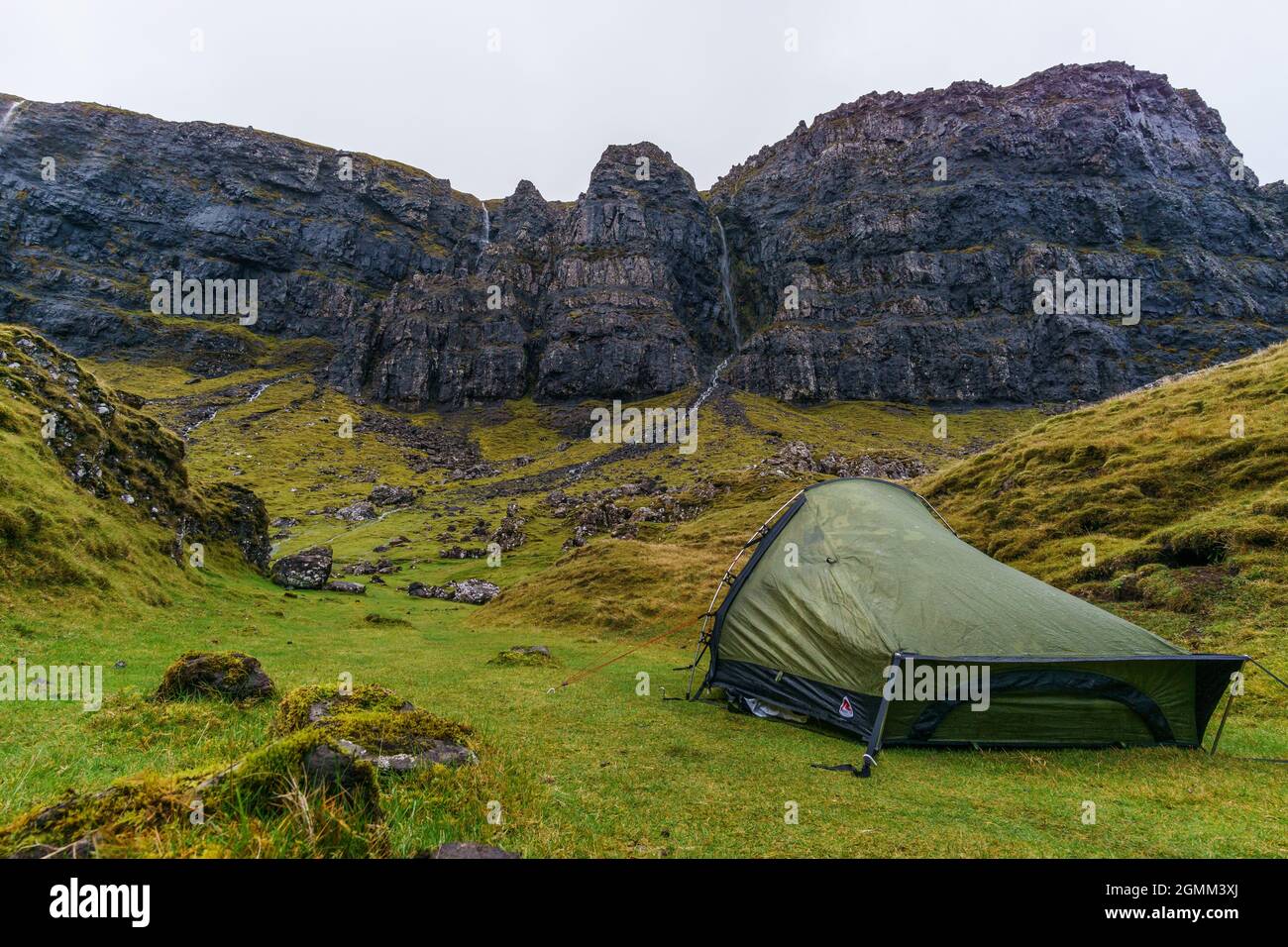 A tent camping in the middle of the green in front of rock formation of ...