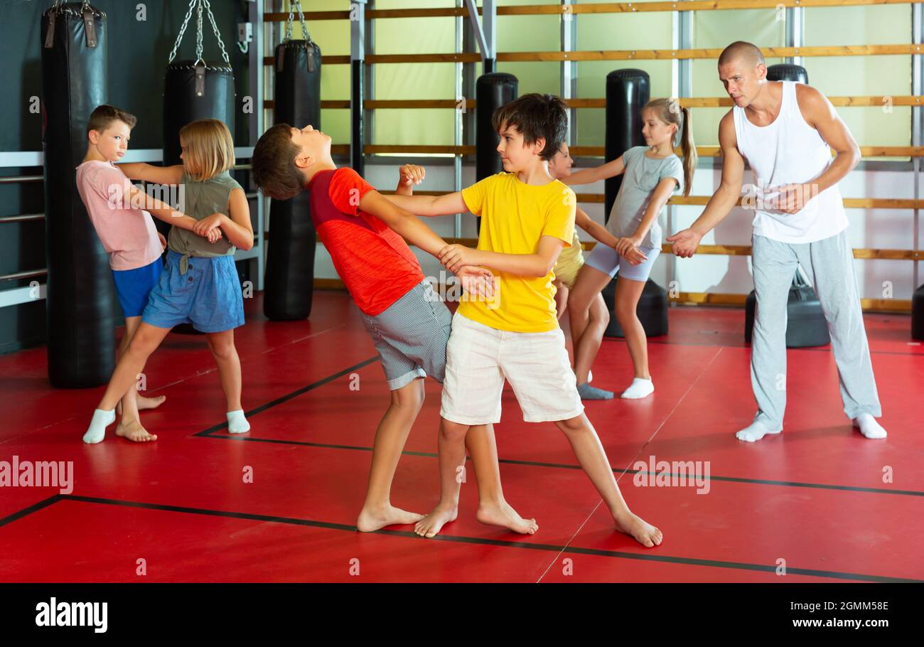 Preteen children practicing in pair self-defence movements with male ...