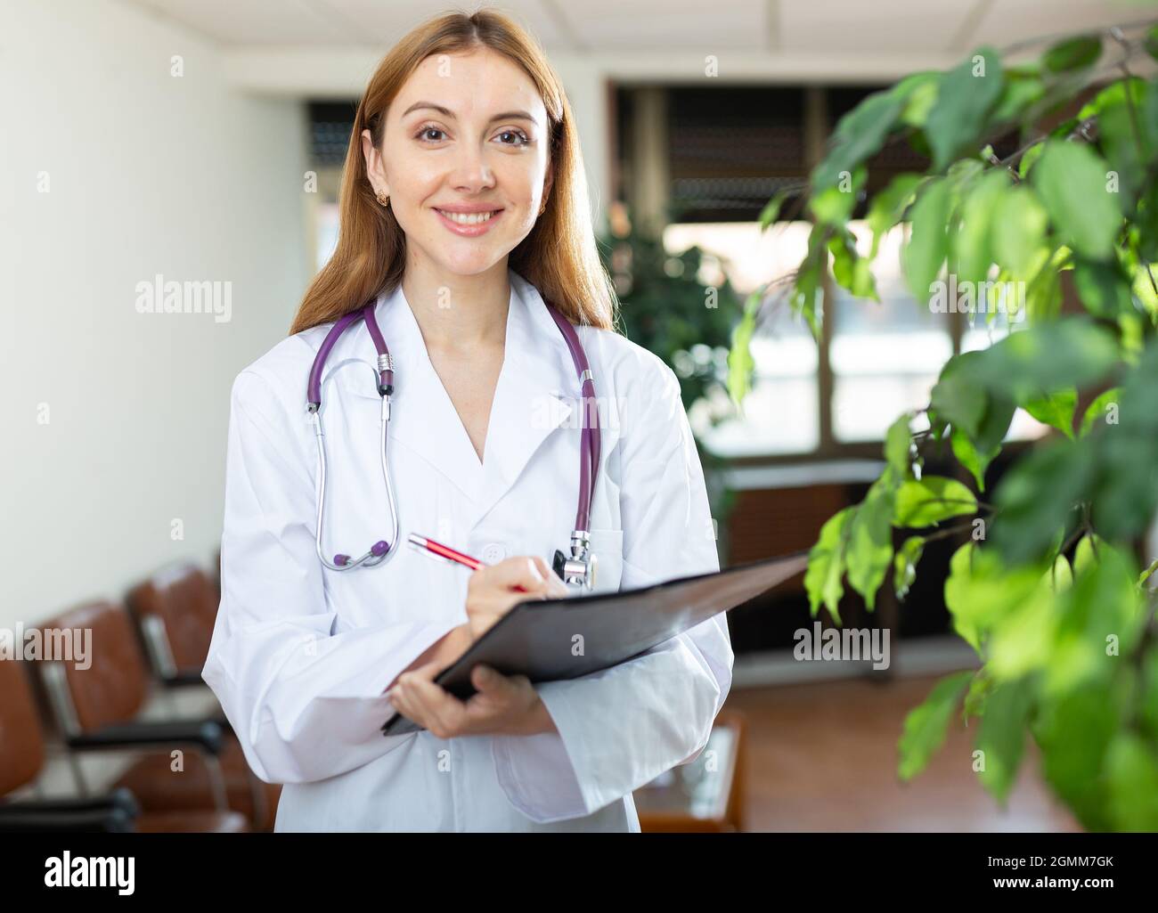 Young woman doctor in white coat filling out medical form at clipboard ...