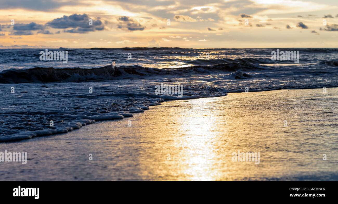 Evening golden hour on the sea beach with dramatic water waves and sun ...