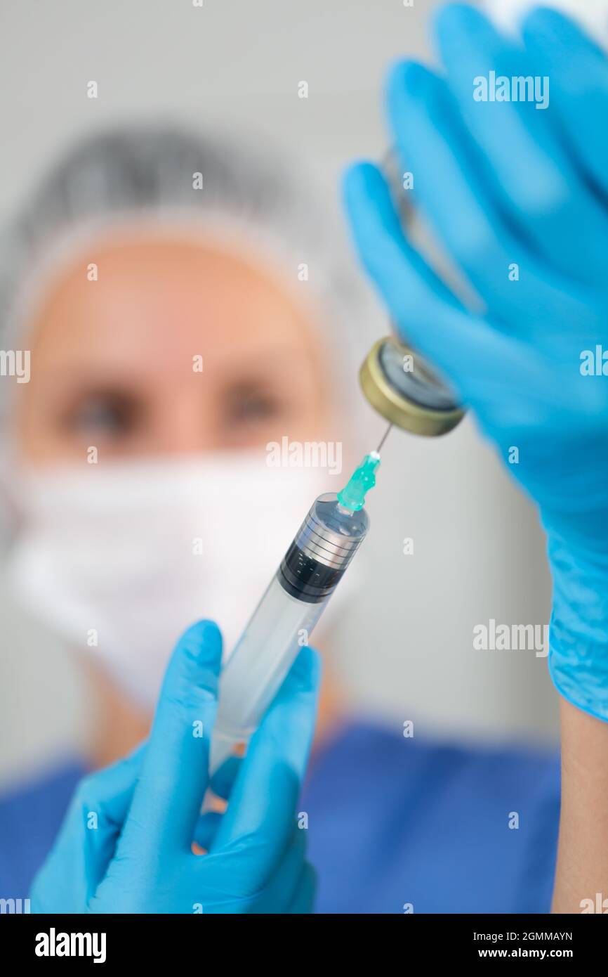 Masked female nurse fills a syringe with saline for injection Stock ...
