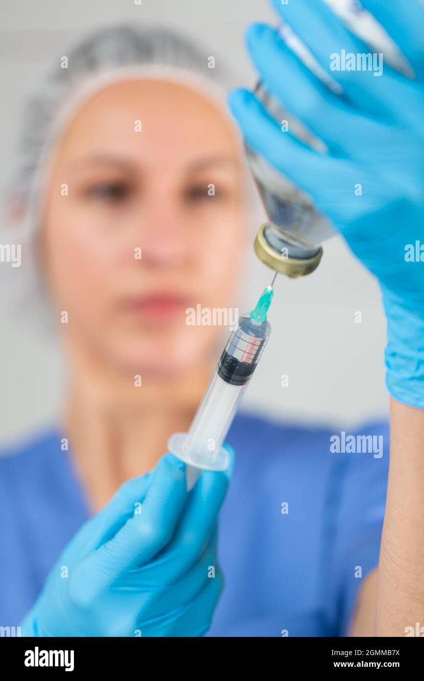 Young female health worker fills a syringe with saline for injection in ...