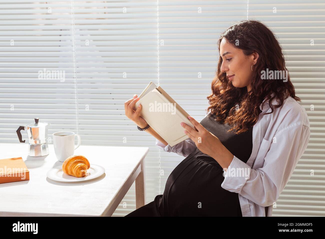 Pregnant woman is reading book while breakfast. Pregnancy and education ...