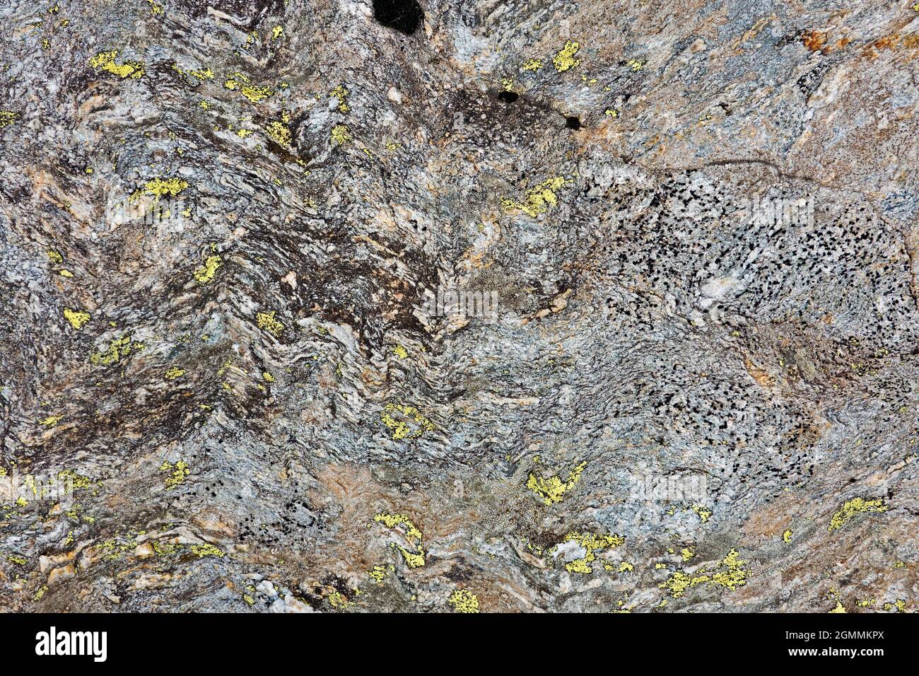 Closeup of grey granite, curved layers and some lichens growing on it ...