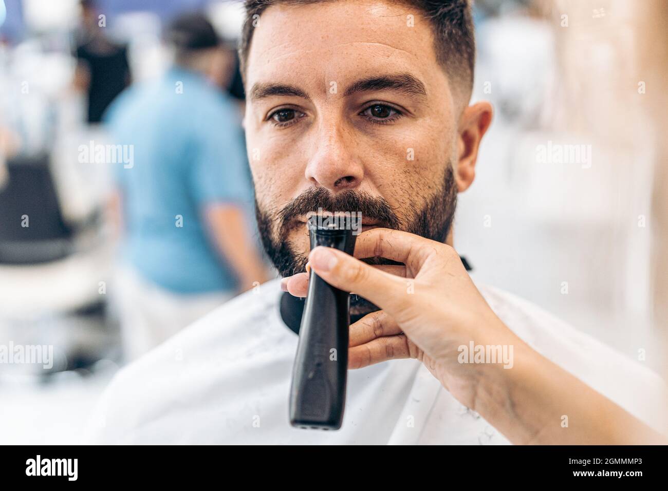 Hand grooming the moustache of a man with an electric razor in a barber ...
