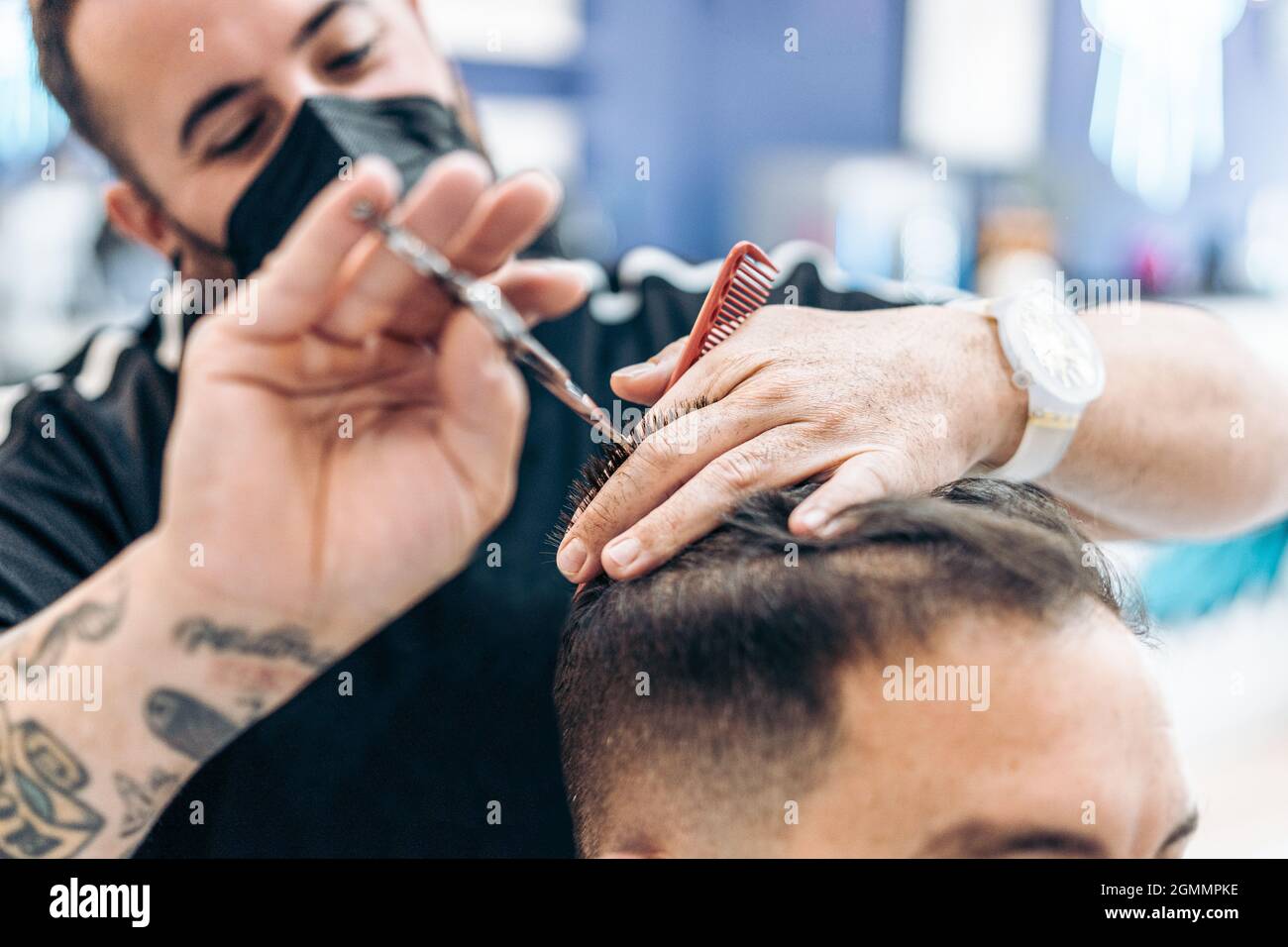 Barber with mask cutting the hair of a client using scissors in a ...