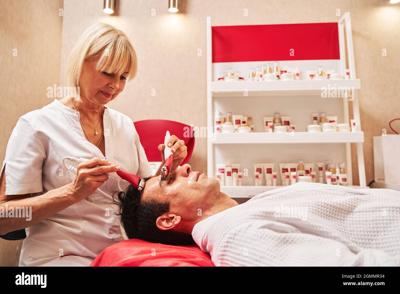 Female massagist doing facial treatment on male face with electricity ...