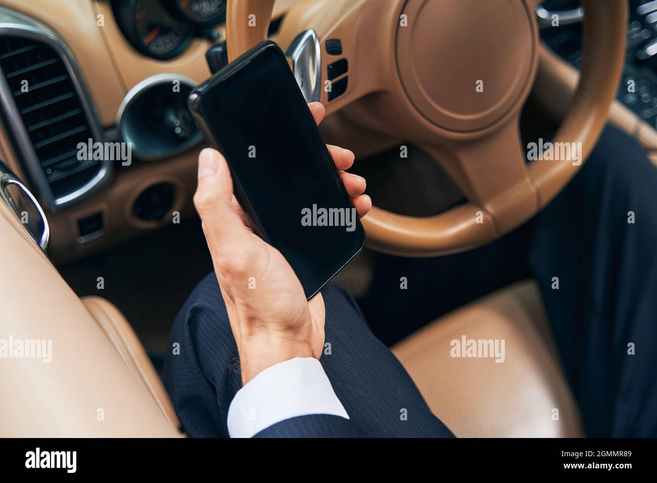 Smartphone in hand in front of steering wheel Stock Photo - Alamy