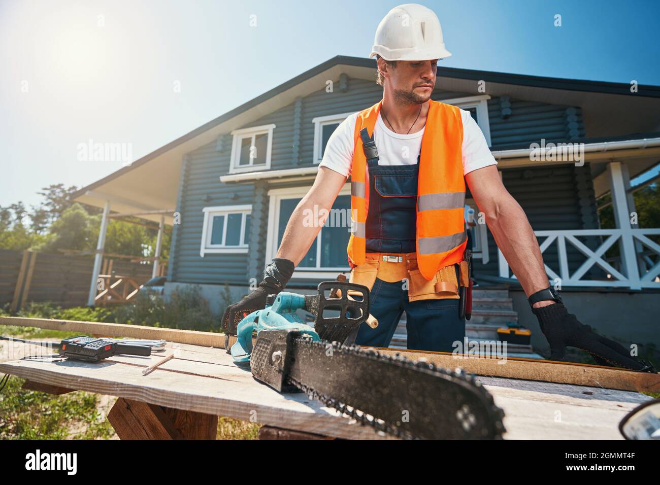 Worker in safety vest grabbing chainsaw from table Stock Photo - Alamy