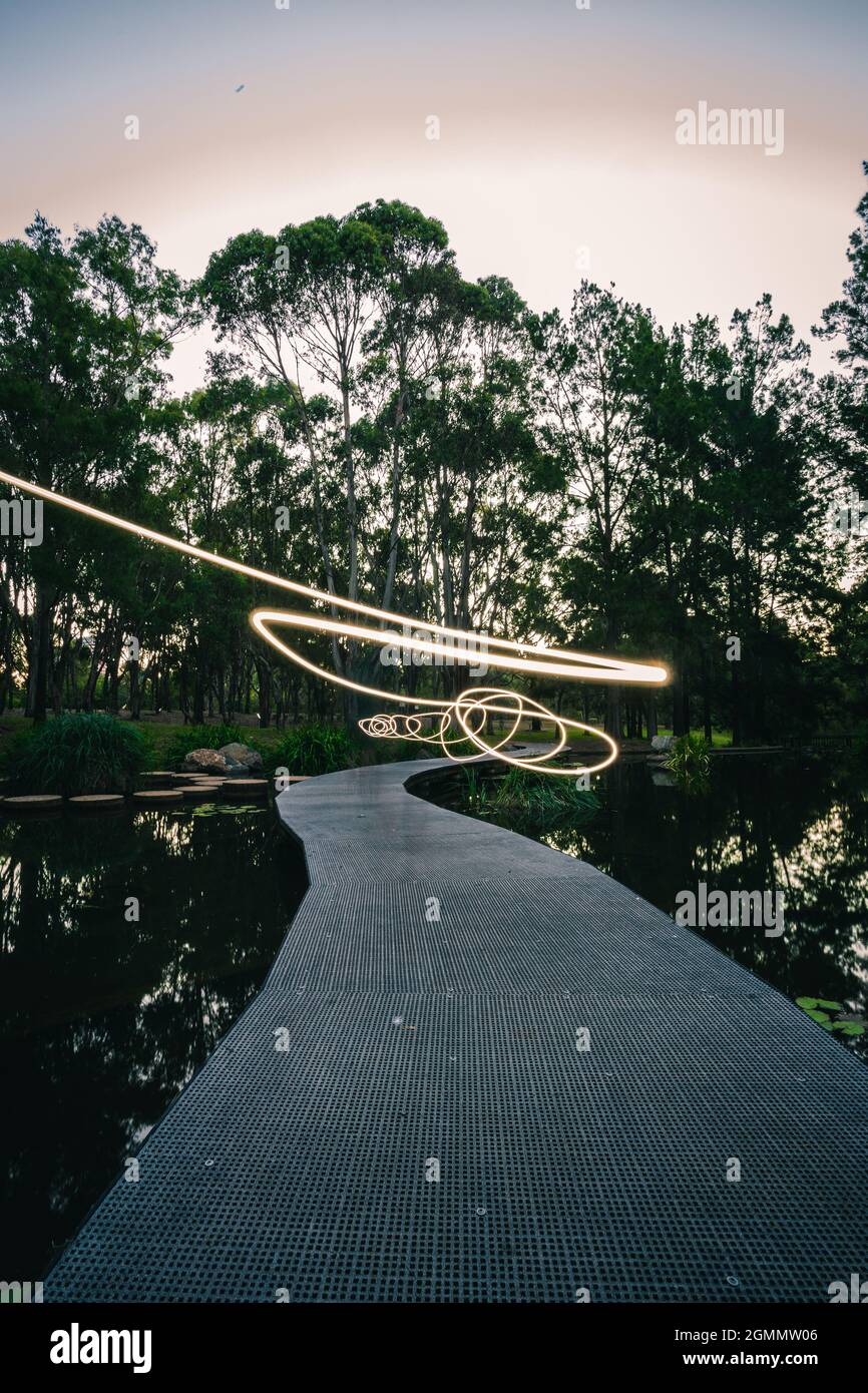 Vertical shot of a lake with a metal path in the park with dense trees ...
