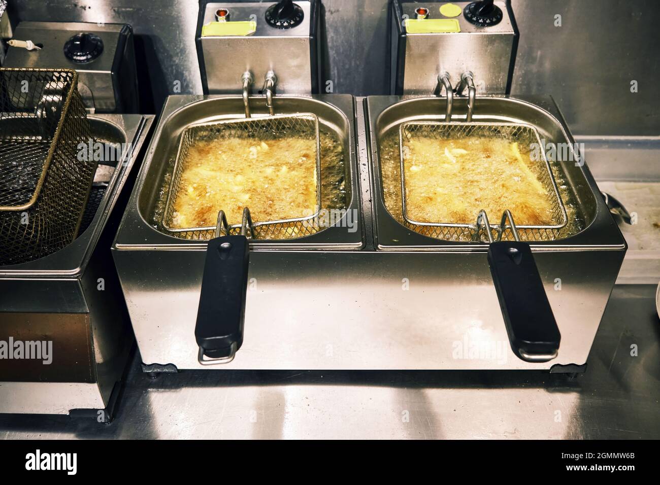 French fries potatoes frying in the hot fryer of a restaurant kitchen ...
