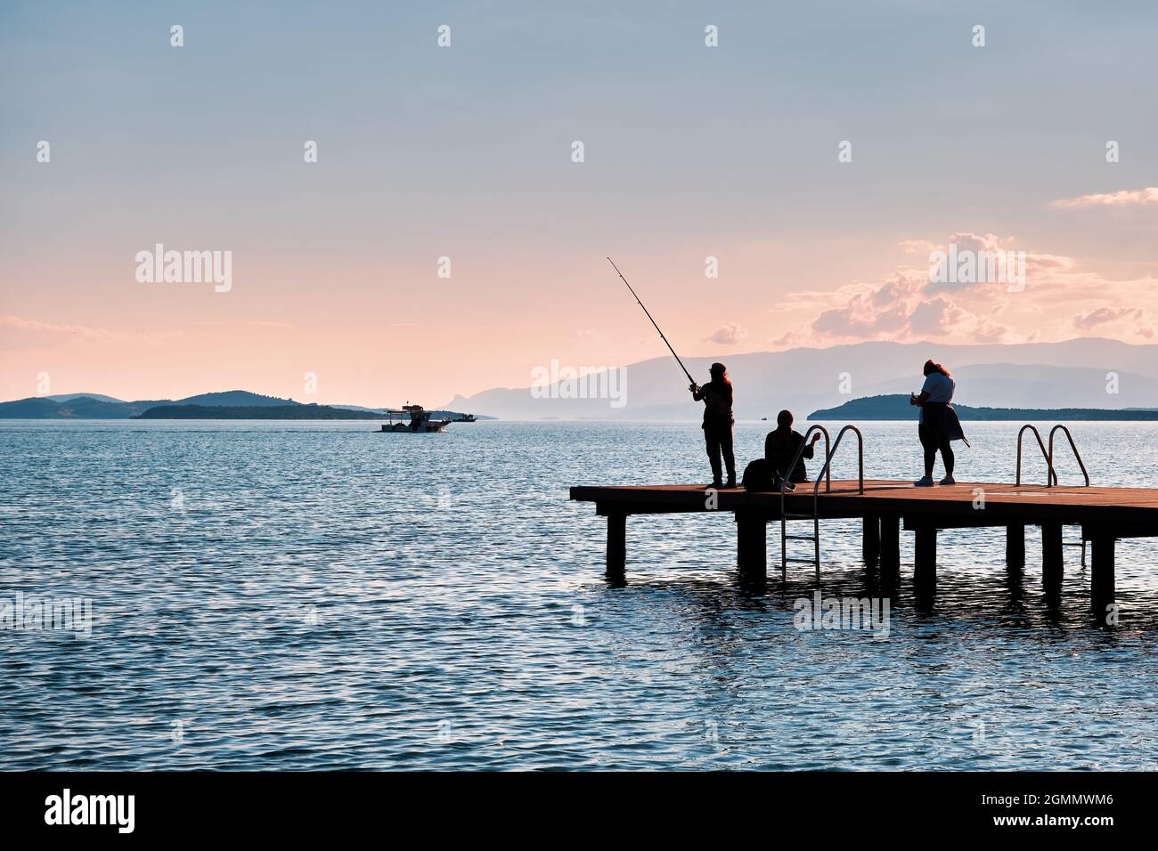 Woman catching fish with a fishing rod on the pier with her friend and ...