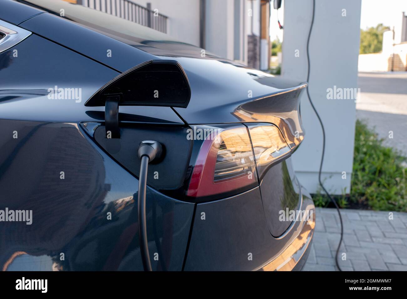 Side view of back part of black electric car with plugged charging ...
