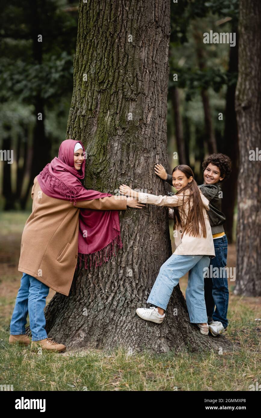 Cheerful muslim woman and children hugging tree in park Stock Photo - Alamy