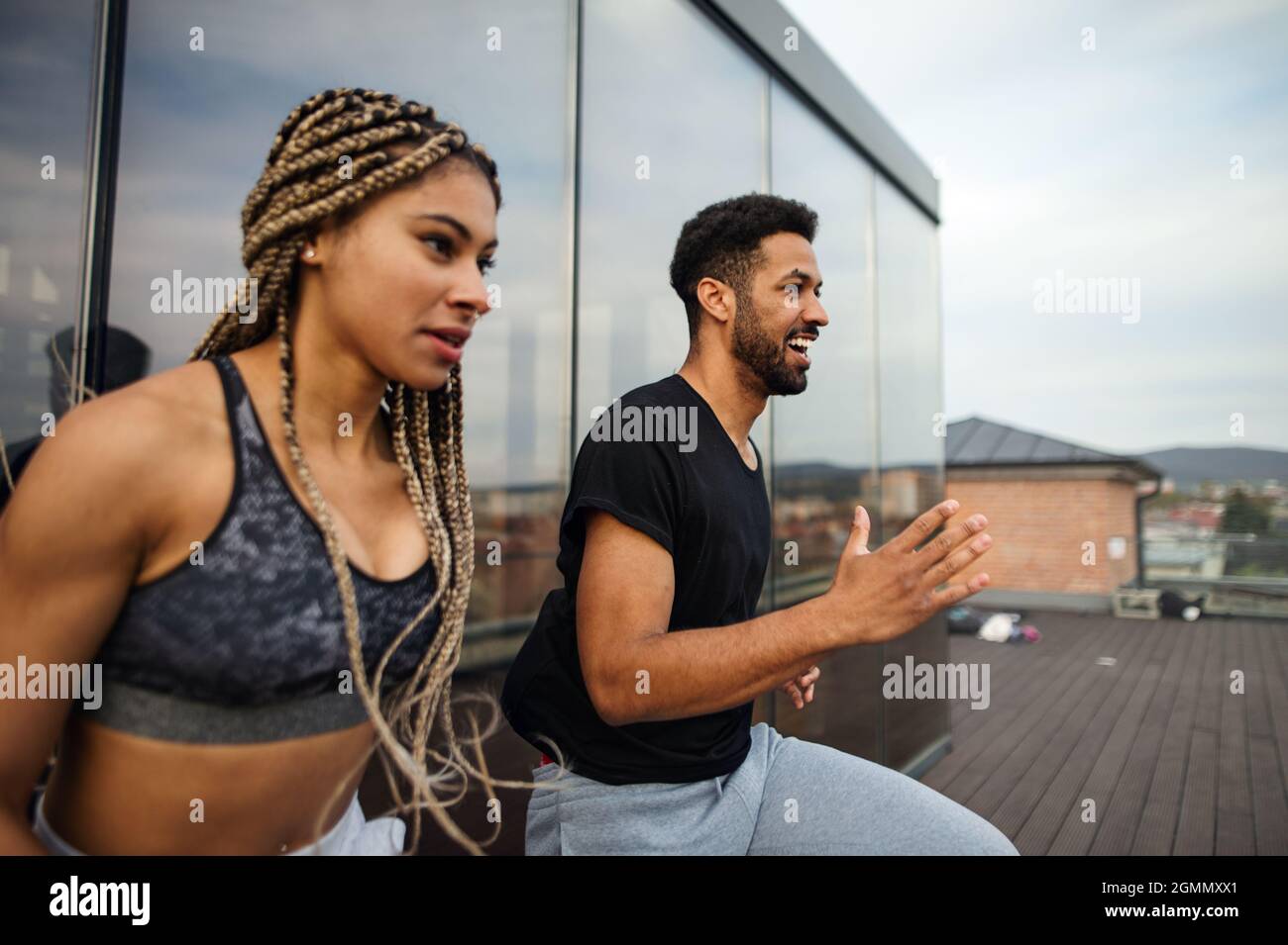 Side view of young couple doing warm up exercise outdoors on terrace ...