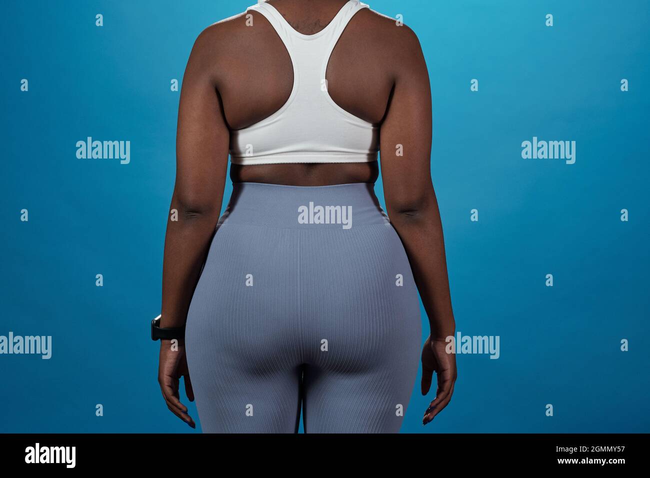 Rear view of young plus size female in activewear standing against blue ...