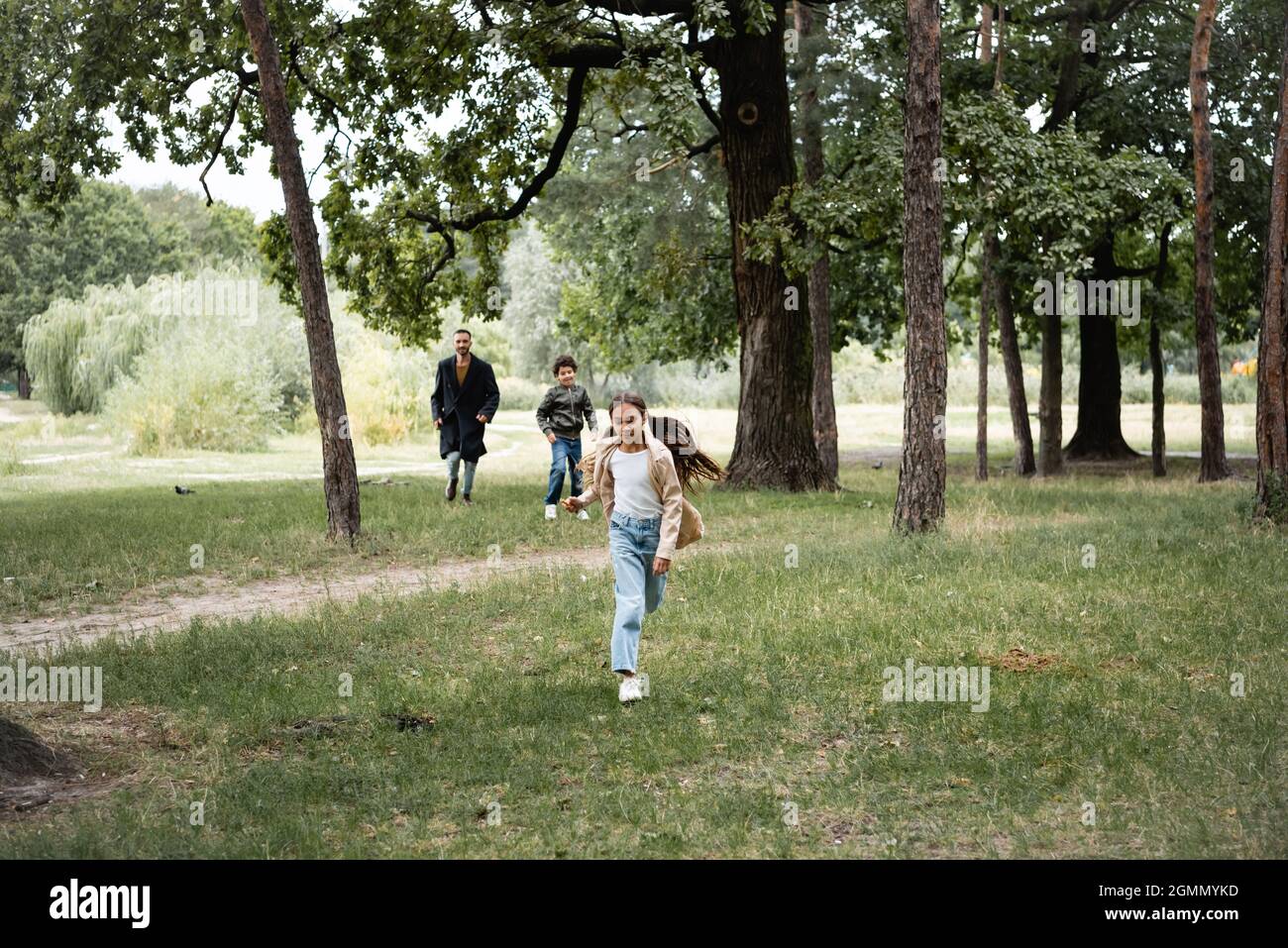 Muslim girl running on lawn near brother and parent in park Stock Photo ...
