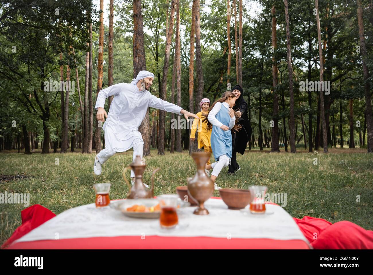 Smiling muslim family running near blurred food and tea in park Stock ...