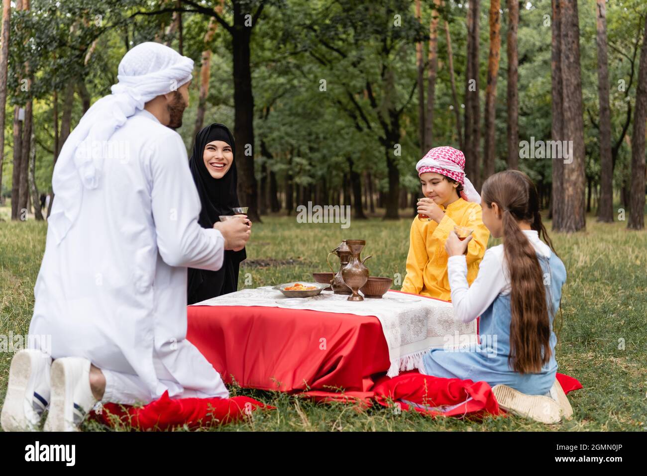 Arabian family holding tea in traditional glasses during picnic in park ...