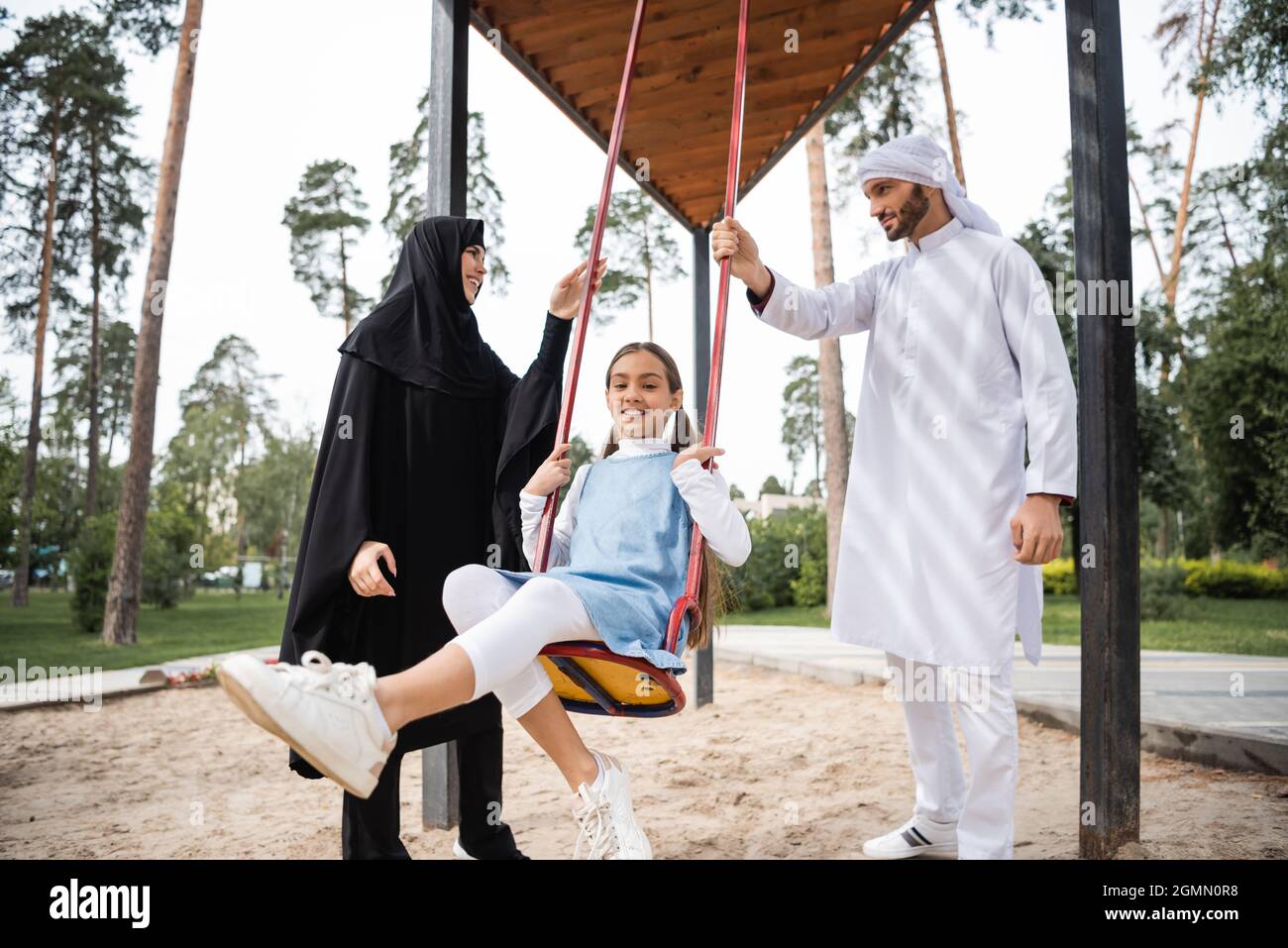 Smiling arabian child on swing near parents in park Stock Photo - Alamy
