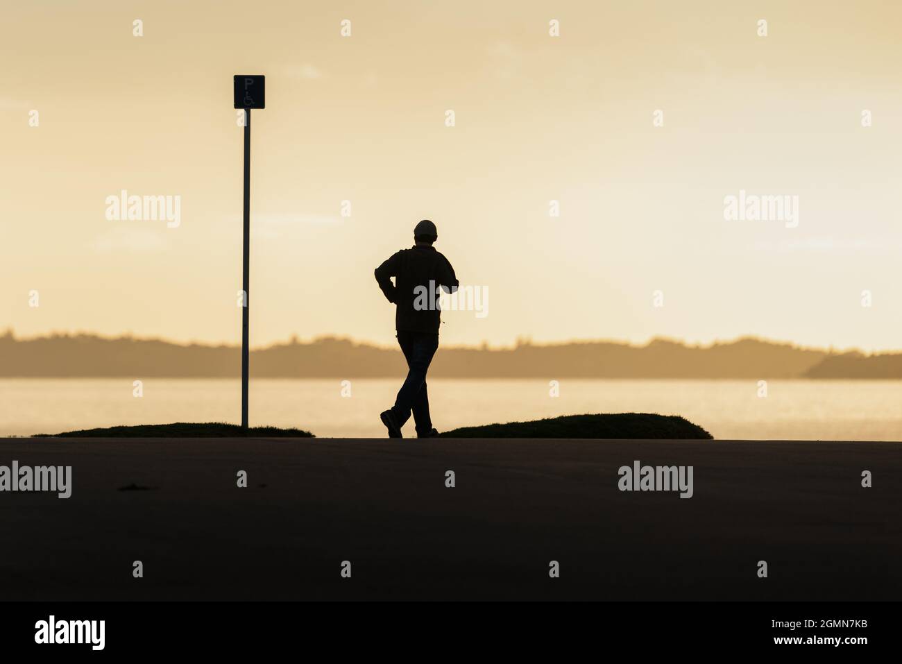 Silhouette of a man running towards the sea with a parking sign post at ...