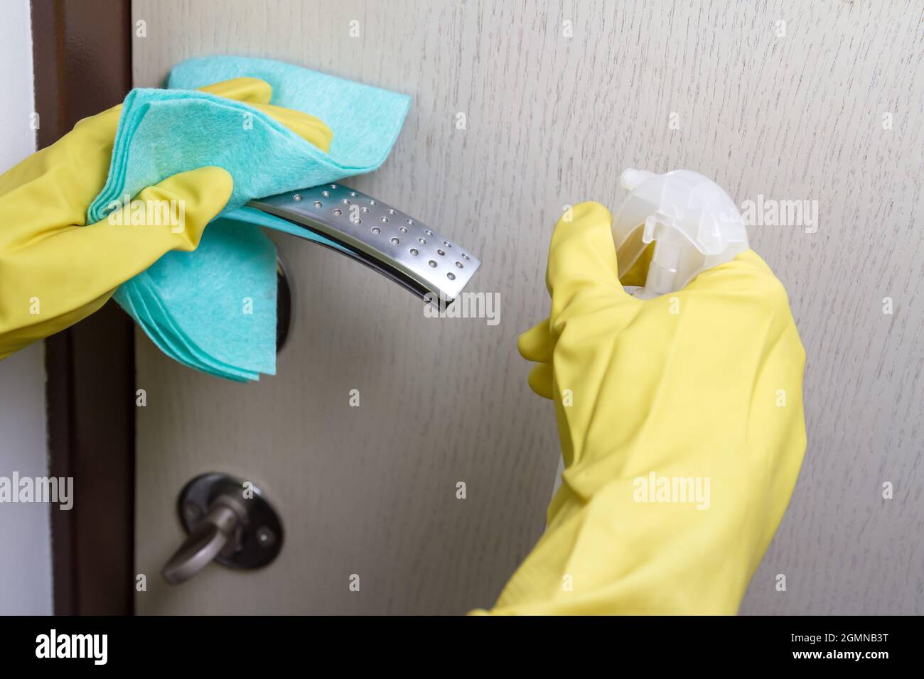 Hands in protective gloves with rag and spray cleaning door handle ...