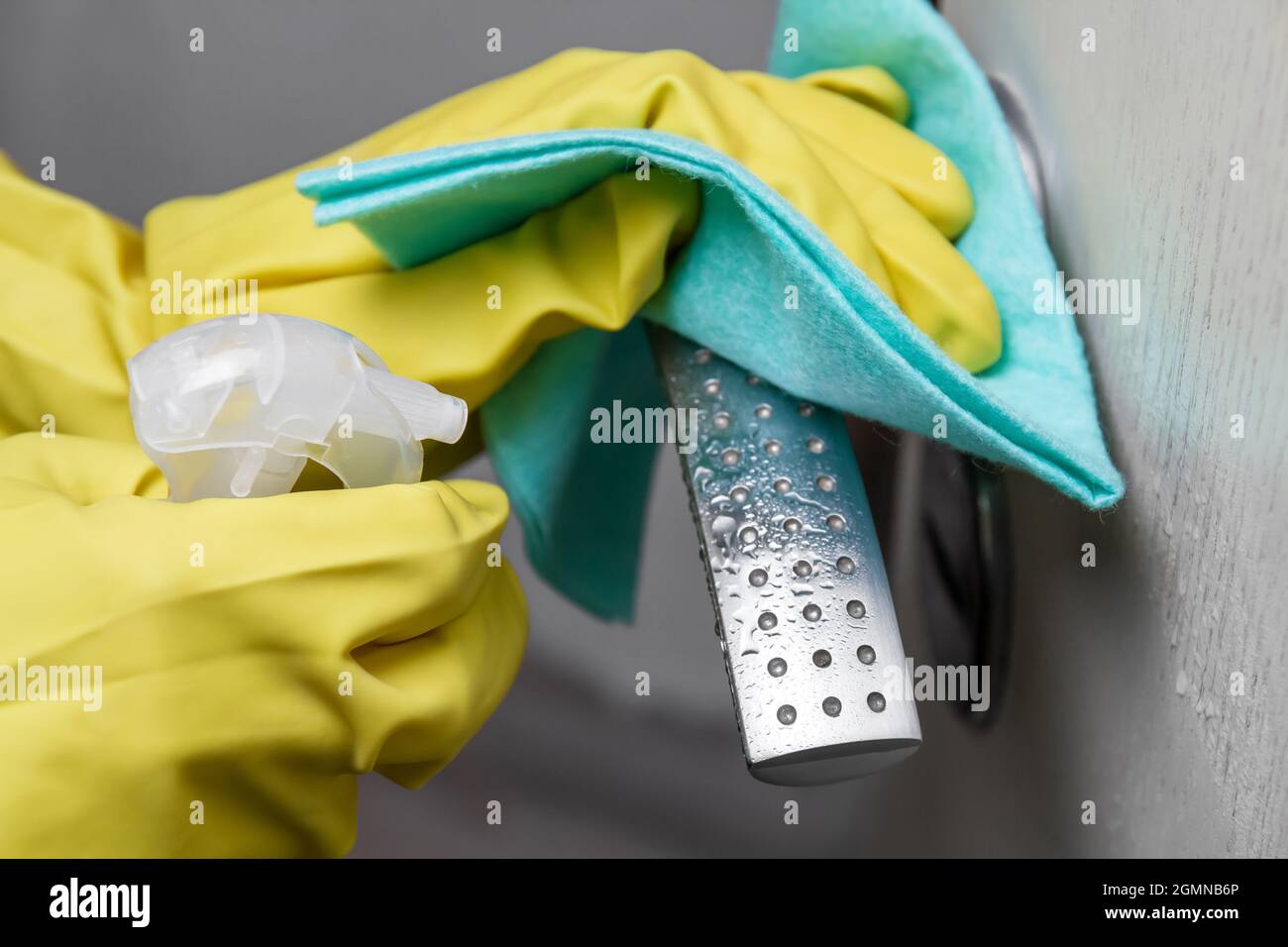Hands in protective gloves with rag and spray cleaning door handle ...
