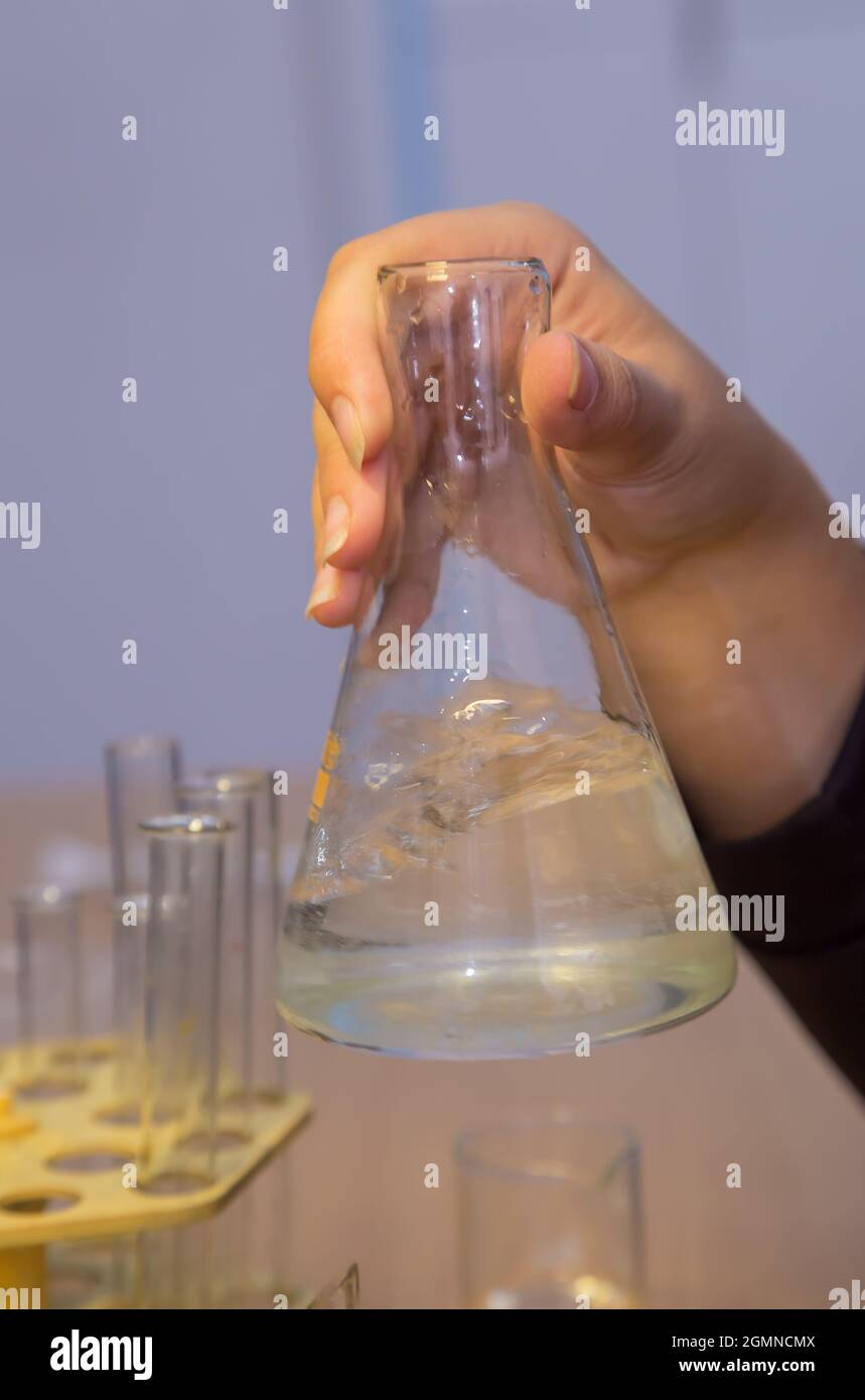 Close-up pupil's hands are shaking a flask with a chemical solution. A ...