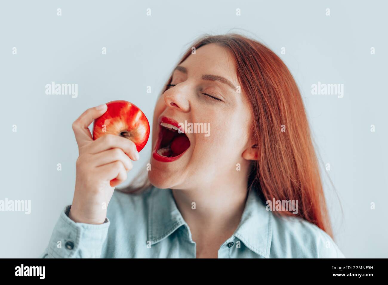 Portrait of a cheerful young woman eating red apple on gray wall ...