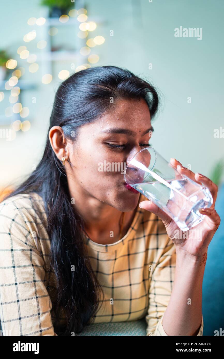 Thirsty young Indian girl drinking glass of pure water during summer ...