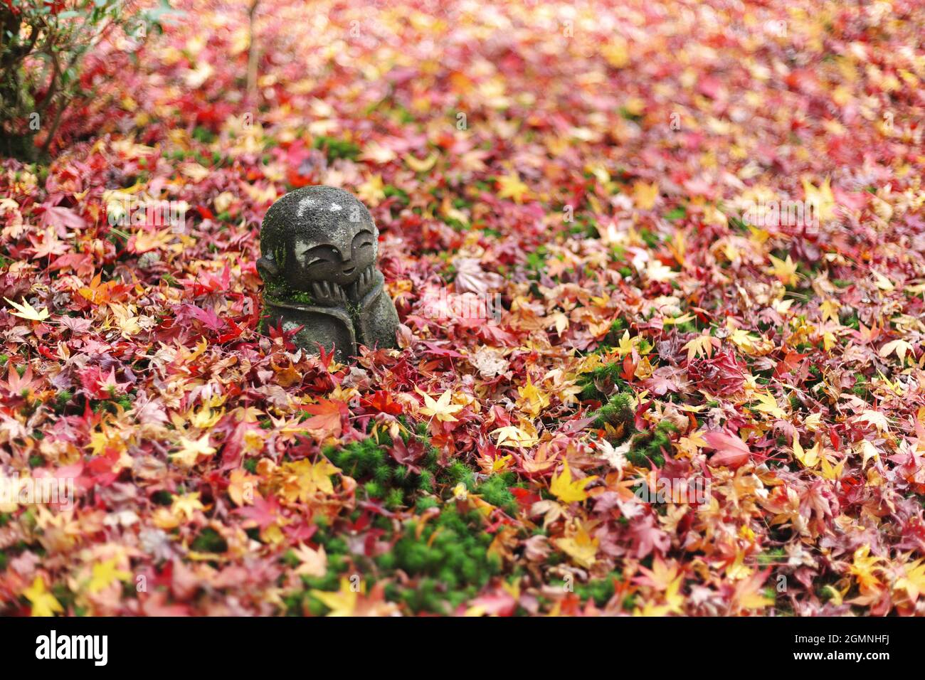 Tiny stone Jizo statue standing on the ground in zen garden covered ...