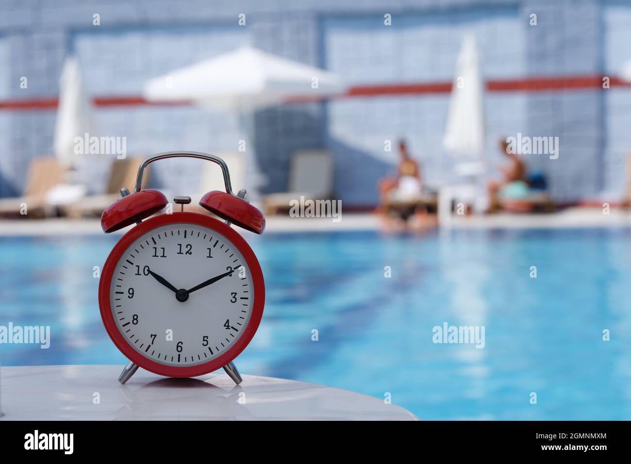 Red analog alarm clock with blurred background of relaxation pool Stock ...