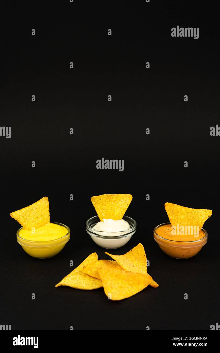 Fast food. Nachos chips with different sauces on a black background ...