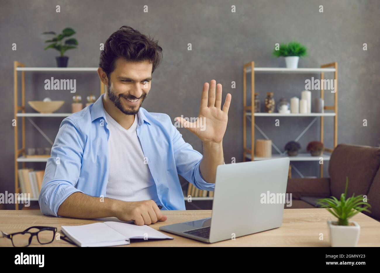 Happy man sitting at desk with laptop computer, smiling and waving hand ...