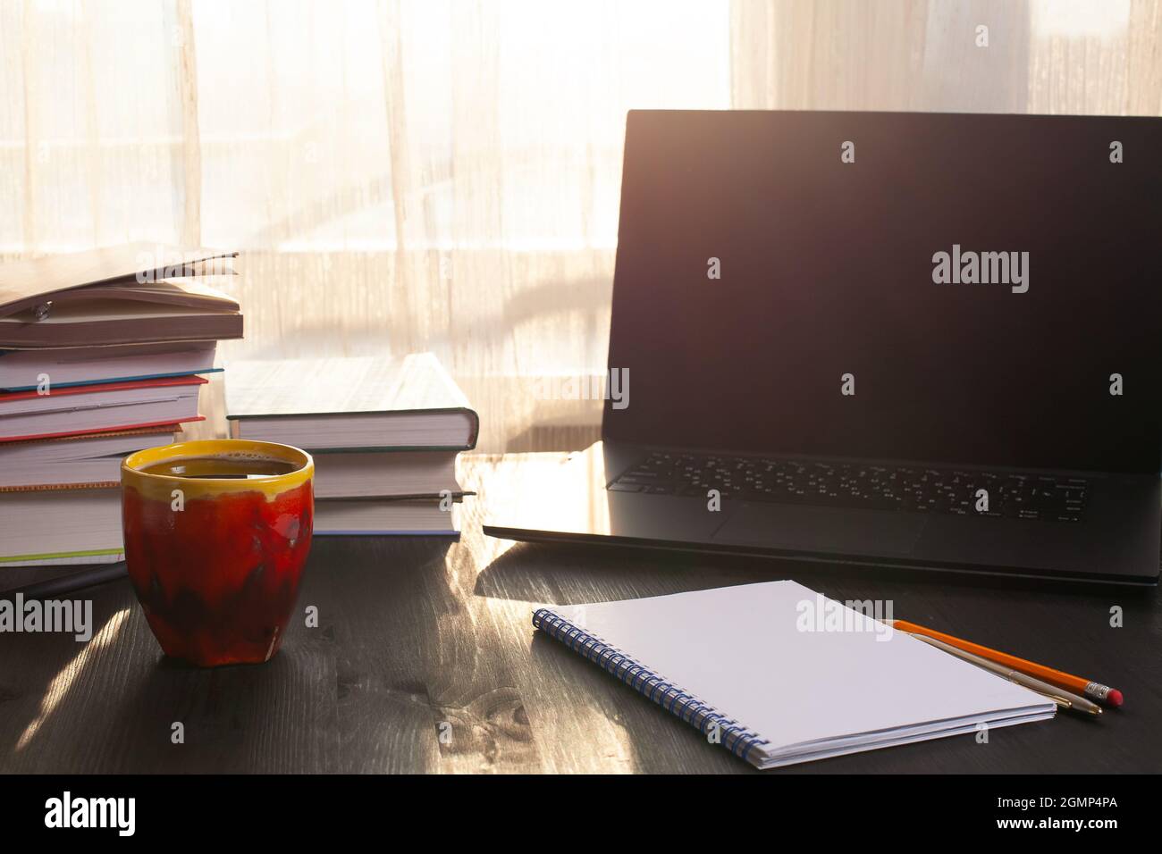 Opened laptop, books and cup of coffee on old wooden desk in morning ...
