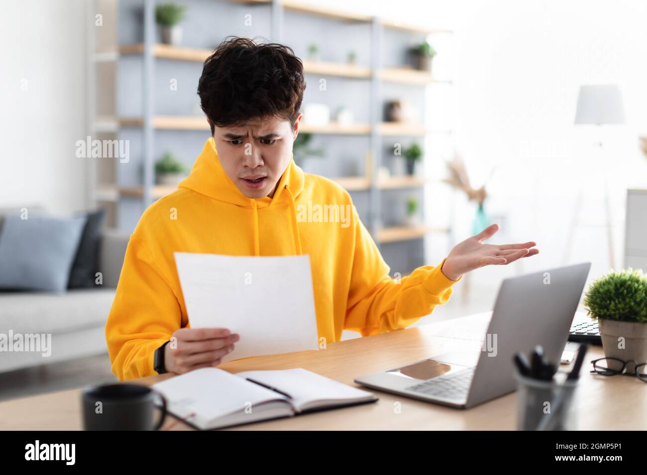 Confused asian man holding paper reading report working on laptop Stock ...