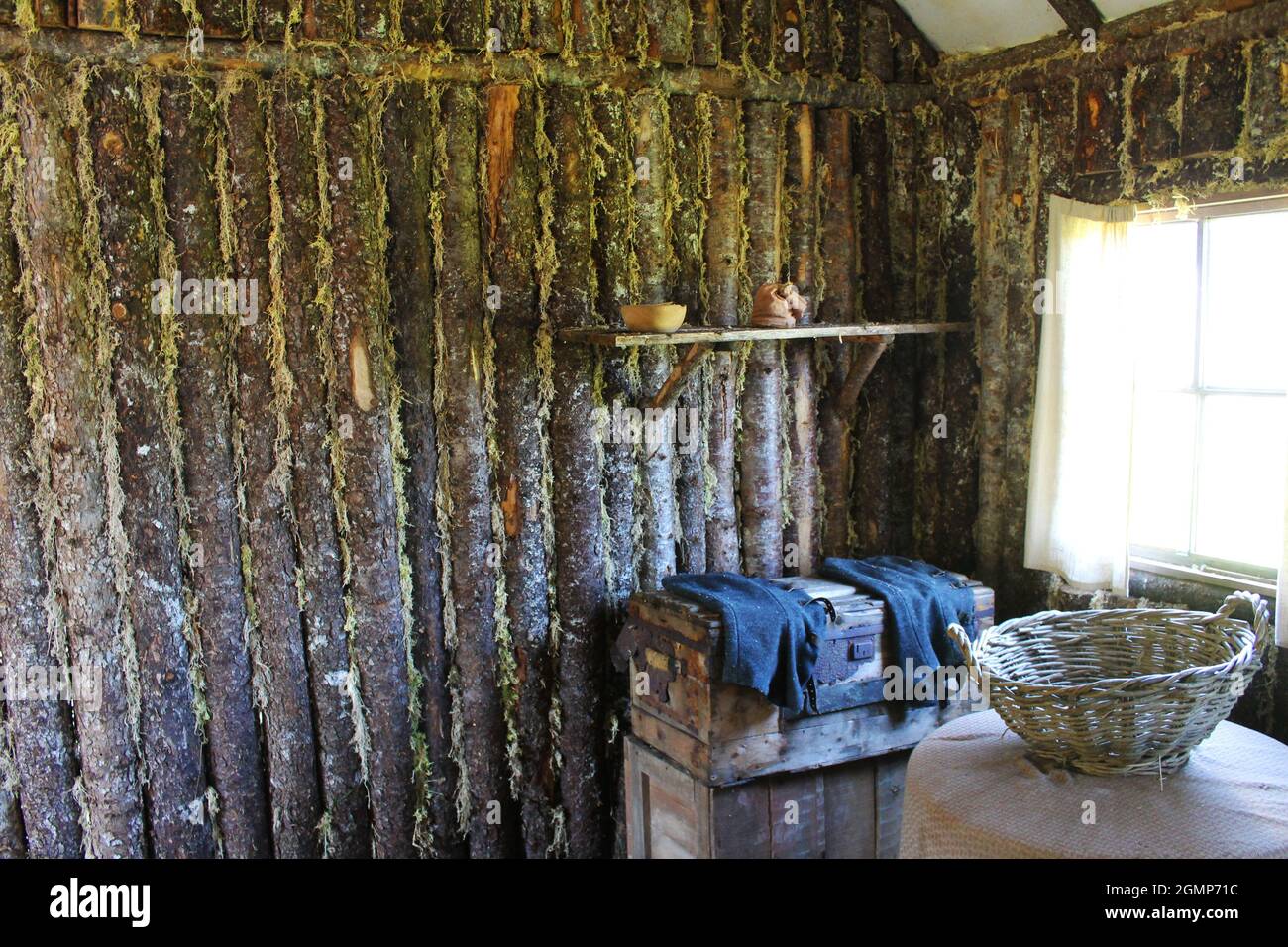 Wooden trunks in a corner, in a log cabin. A table with a straw basket ...