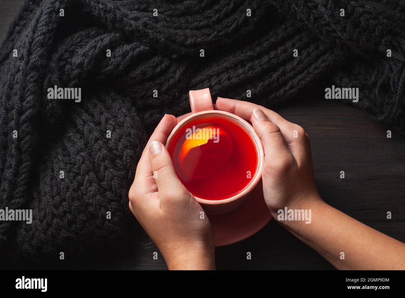 Hands holding tea cup with lemon on dark background. Black knitted ...