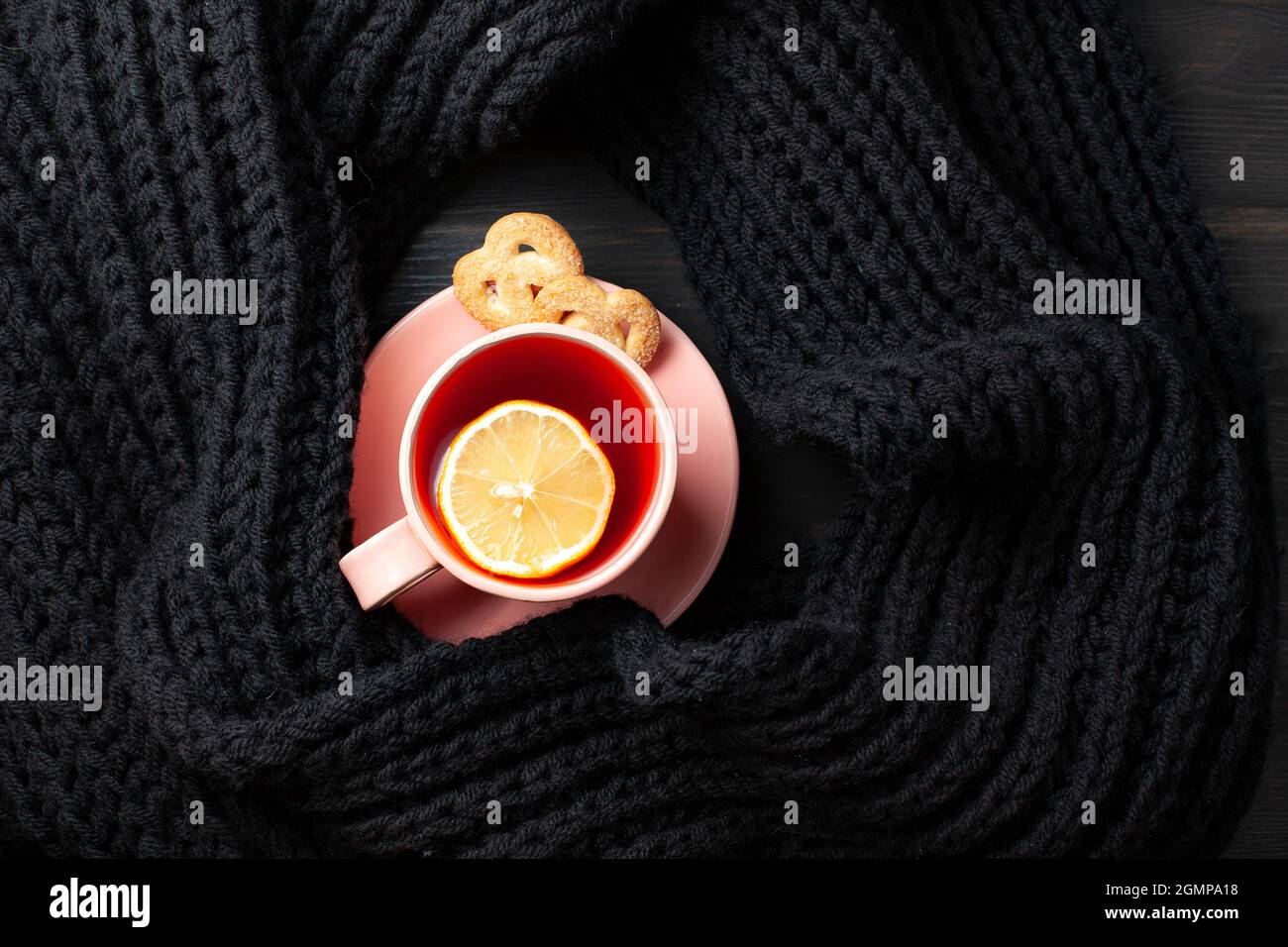 Pink cup of hot tea with lemon and knitted scarf on black wooden ...