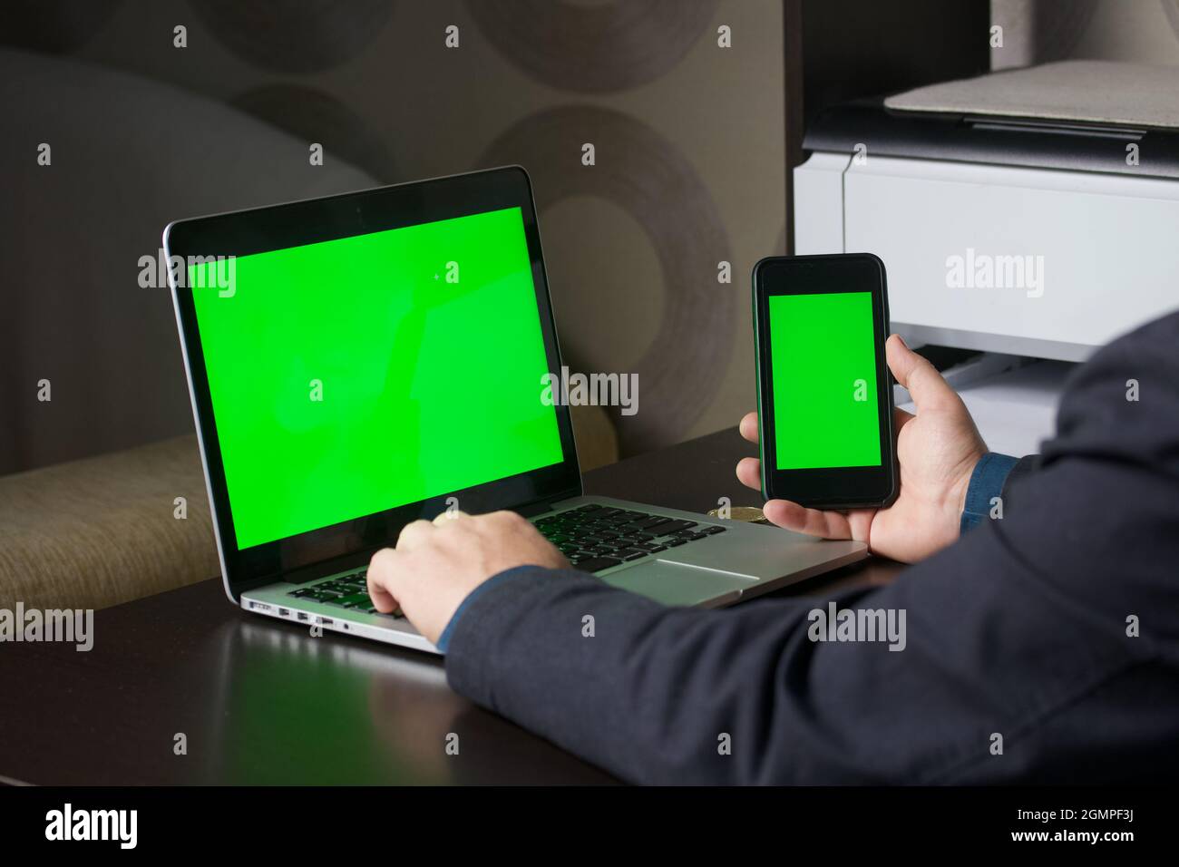 A man works at a laptop with a green screen. He holds a smartphone with ...