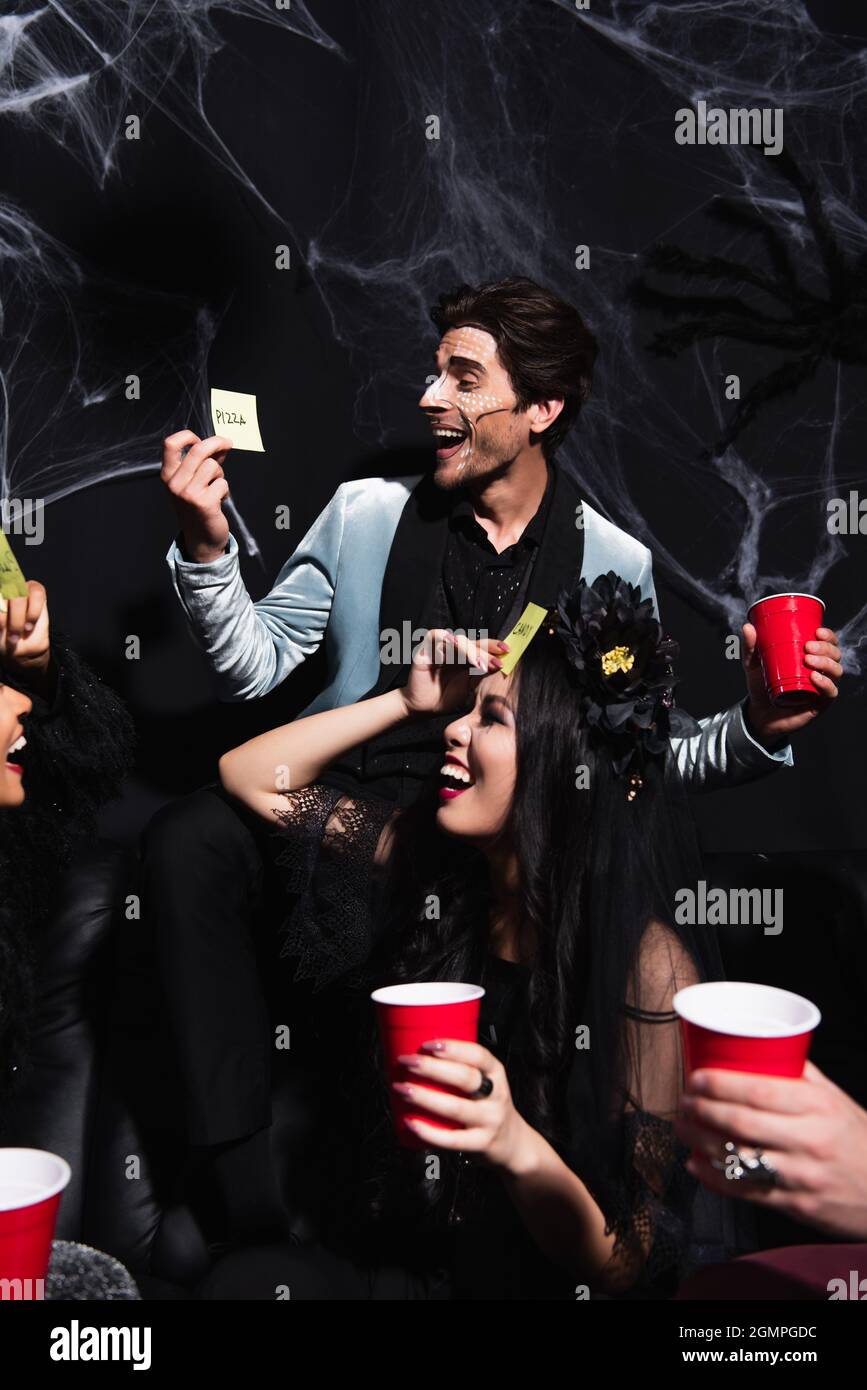 cheerful man looking at sticky note while playing guess who game with ...